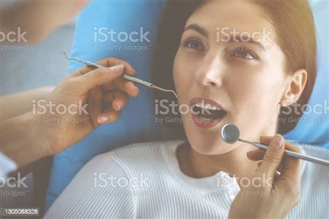 치과 진료소에서 치과 의사에 의해 검사되는 웃는 갈색 머리 여자 환자의 입 근처에 치과 기구를 들고 의사의 손 건강한 치아 및