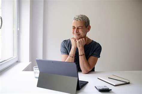 책상 옆 하얀 사무실에 앉아 짧은 머리로 노트북으로 작업하는 예쁜 중년 여성 40 49세에 대한 스톡 사진 및 기타 이미지