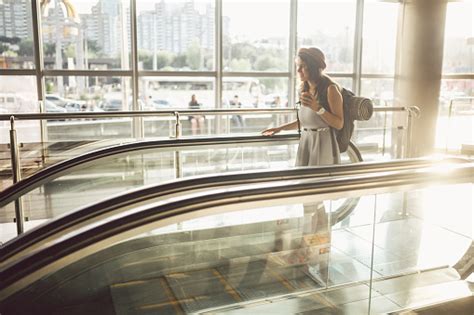 에스컬레이터에서 공항에서 모자를 쓰고 웃는 모습 기내 수하물을 가지고 여행하는 사람들 테마 관광 및 교통 에스컬레이터에 공항 터미널에서 커피와 백인 소녀 가방에 대한 스톡