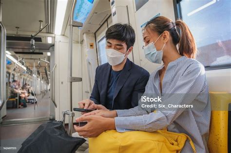 두 명의 아시아 사업가 동료 또는 부부가 휴대 전화를 사용하여 보호 얼굴 마스크를 착용하고 Bts 스카이 트레인 또는 Mrt