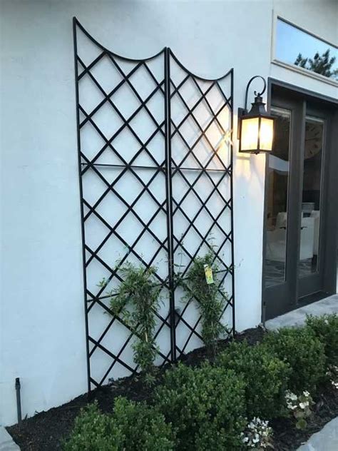 An Iron Trellis On The Side Of A Building With Plants Growing Out Of It
