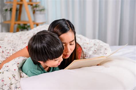 아시아의 어머니는 아들과 함께 집으로 일합니다 엄마와 아이는 침대에서 잠들기 전에 동화를 읽는다 여성의 라이프 스타일과 가족