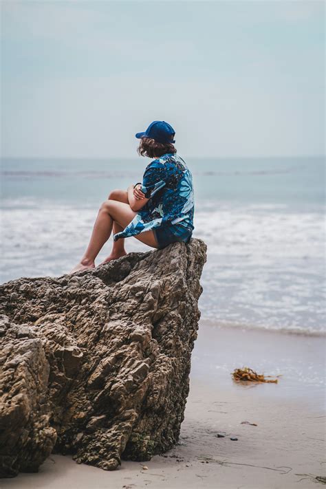 Woman In Blue And White Floral Dress Sitting On Rock Near Sea During