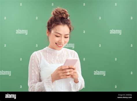 Happy Young Beautiful Typing On Mobile Phone While Standing Isolated Over Green Background Stock