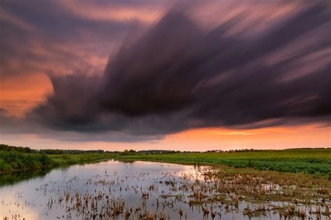 Green Grass Field Near Body Of Water Under Cloudy Sky During Daytime