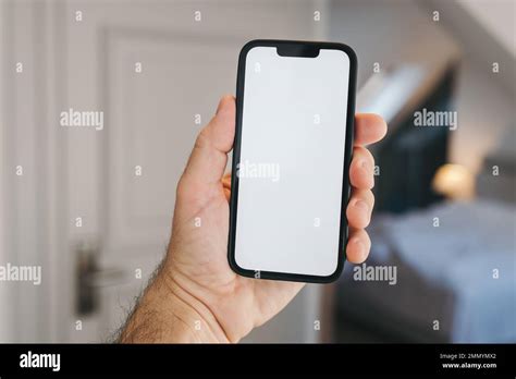 Tourist In Hotel Bedroom Holding Smartphone With Blank Mockup Screen