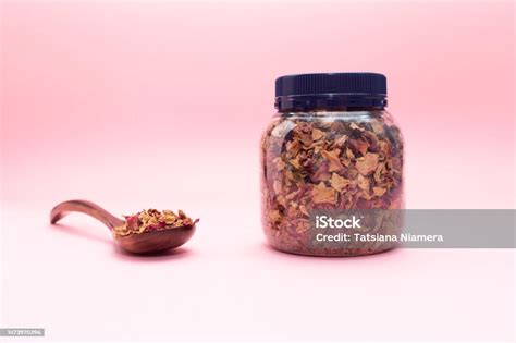 항아리 말린 장미 꽃잎이 든 플라스틱 용기 나뭇잎 분홍색 배경에 건조된 장미로 채워진 나무 숟가락 향기로운 꽃 봉오리로 만든