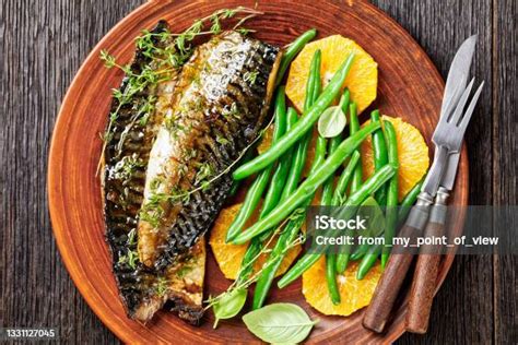 오렌지 유약 고등어 필레의 오버헤드 뷰에 신선한 오렌지와 찐 녹색 콩이 있는 소박한 점토 접시에 칼붙이가 달린 부드러운 나무 테이블에 평평한 평지 클로즈업 0명에 대한 스톡