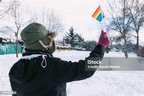레즈비언 여자 뒤에서 입고 A 머리 눈 모자 에 A 눈 덮인 지역 들고 Lgbt 무지개 플래그 겨울에 대한 스톡 사진 및 기타