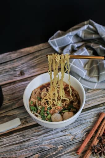 손은 젓가락을 사용하여 돼지고기와 채소를 곁들인 맛있는 달걀 국수를 나무 테이블 탑 뷰아시아 음식 스타일로 5가지 향신료 블랙 수프에 들어오릅니다 5가지 개체에 대한 스톡