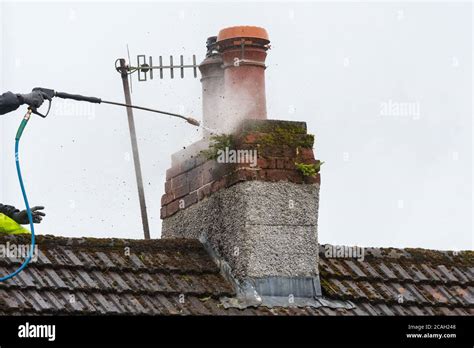 Man Power Washing A Chimney Stack And Roof To Remove Dirt Moss And