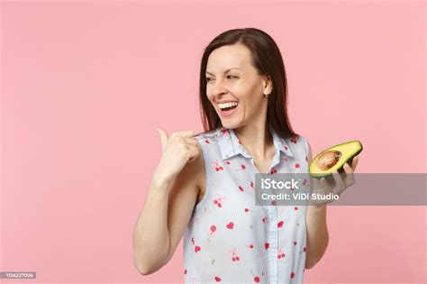 여름 옷을 옆에 젊은 여자를 웃 고 밖으로 분홍색 파스텔 배경에 고립 된 신선한 잘 익은 아보카도 과일의 절반을 잡아 사람들은