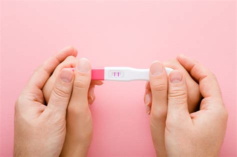 젊은 여자와 남자 손 함께 임신 테스트를 들고 두 줄무늬 밝은 분홍색 테이블 배경에 파스텔 색상 긍정적 인 결과 근접 촬영 관점