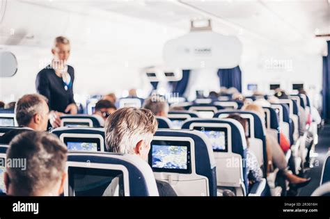 Interior Of Airplane With Passengers On Seats And Stewardess In Uniform
