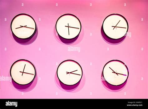 six analog wall clocks displaying different times on a vibrant pink