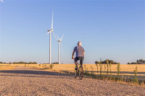 모자를 쓴 남자와 풍력 발전 타워가 있는 시리얼 밭 옆에서 자전거를 타는 남자의 뒷모습 풍력에 대한 스톡 사진 및 기타 이미지 풍력 발전소 여름 Istock