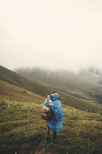 세련 된 Hipster 소녀 파란색 비옷에 배낭에 산 위에 안개가 자욱한 언덕을 보고 산을 탐험 하는 젊은 여성 여행자 여행과