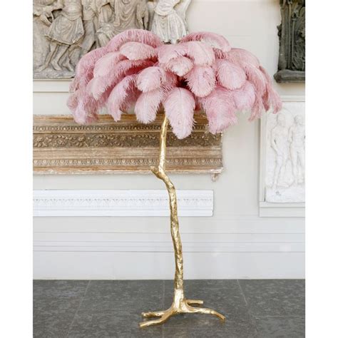 A Pink Ostrich Feather Lamp In Front Of A Wall With Statues Behind It