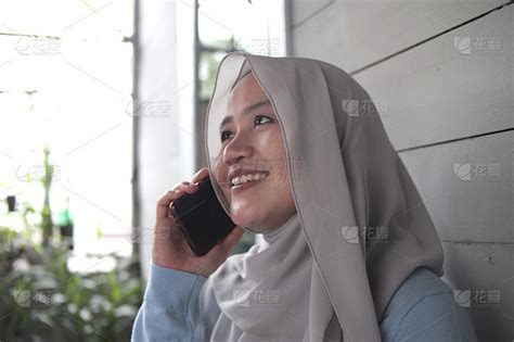 快乐的亚洲穆斯林妇女在她的家外面打电话，笑得很开心