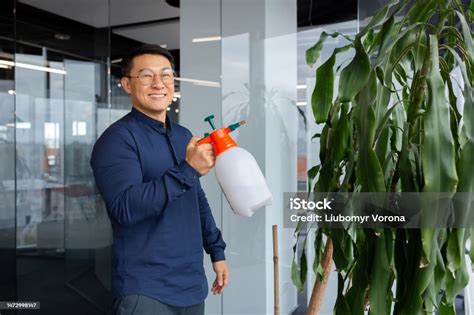 사무실 안에서 성공적으로 웃고 있는 아시아 남자의 초상화 분무기로 화분을 뿌리는 꽃에 물을 주는 상사 웃고 카메라를 바라보는 사업가 캐주얼 셔츠를 입은 보스 35 39세에