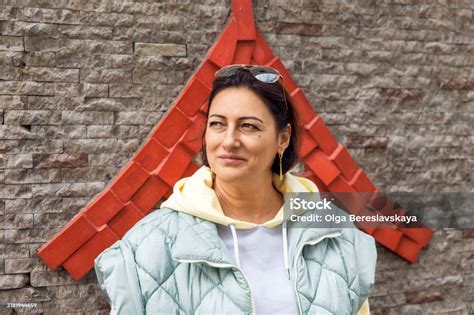 캐주얼 한 복장을 한 여자가 붉은 악센트가 있는 질감이 있는 돌담 옆에 서 있습니다 45 49세에 대한 스톡 사진 및 기타 이미지 45 49세 개성 개념 거리