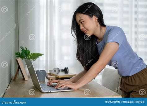 A Beautiful Asian Woman Bending Over A Table And Using Her Laptop
