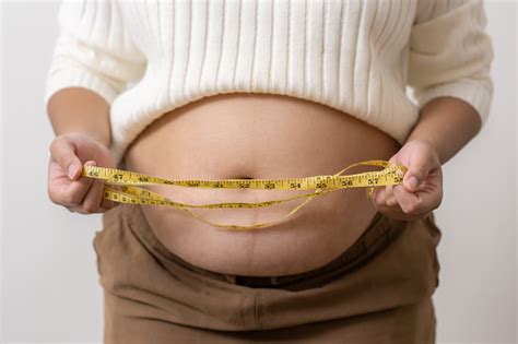 실제 크기를 보여주기 위해 측정 테이프를 사용하는 비만 배꼽에 측정 테이프를 사용하는 통통한 뚱뚱한 여자 임신 후 여성의 실제