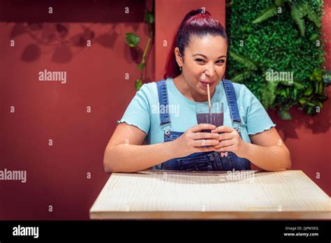 Joyful Young Woman Enjoying Drinking A Fresh Smoothie While Sitting At