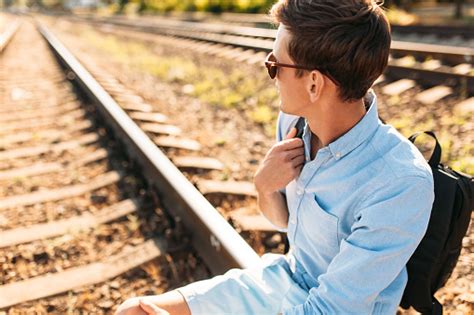 아름 다운 세련 된 남자 안경 일몰 Hipster 세련 된 옷 광고 텍스트 삽입에 대 한 포즈에 열차의 레일에 앉아 포즈