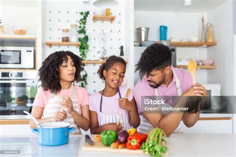 쾌활한 젊은 부모와 어린 딸이 부엌에서 함께 굽는 동안 즐거운 시간을 보내고 행복한 아프리카 계 미국인 가족이 노래하고 바보짓을하고 주걱을 사용하여 마이크를 털고 공간을