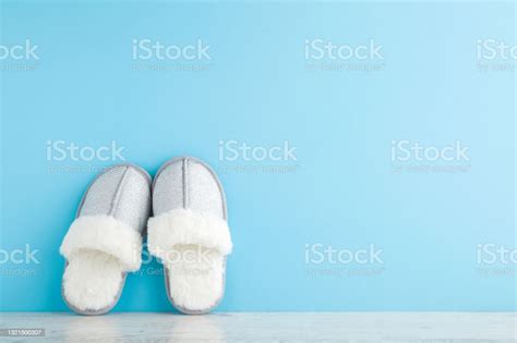 밝은 파란색 벽 배경의 나무 바닥에 흰색 모피가있는 아름다운 부드러운 따뜻한 여성 회색 슬리퍼 파스텔 색상 근접 촬영 편안한 홈