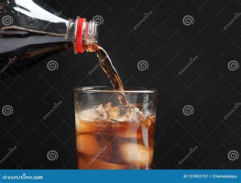 Pouring Refreshing Cola From Bottle Into Glass With Ice Cubes On Black