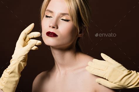 Naked Blonde Girl With Closed Eyes And Human Hands In Yellow Gloves On Brown Stock Photo By