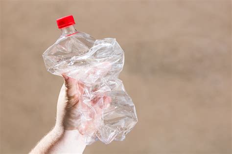 손으로 들고 흐린 배경에 고립 된 빈 플라스틱 병을 박살 재활용 및 자원 봉사 개념 환경 오염 및 전 세계 생태 문제 개념에