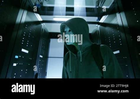masked hacker in a hoodie walks through corporate data center with rows