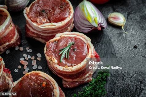 베이컨으로 싸인 생 돼지고기 메달리온 스테이크는 향신료 소금과 후추 최고 전망과 어두운 콘크리트 배경의 슬레이트 보드에 제공됩니다 건강한 생활방식에 대한 스톡 사진 및 기타