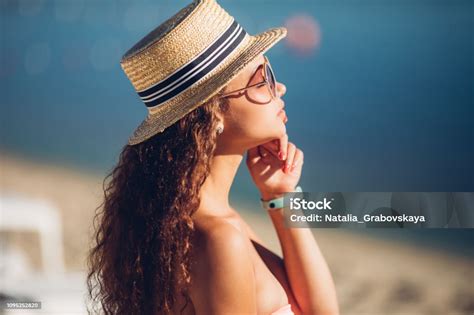 바다 바람을 즐기는 행복 한 생강 여자의 근접 야외 초상화 바다에 Photoshoot를 즐기는 모자에 긴 검은 머리와 매력적인