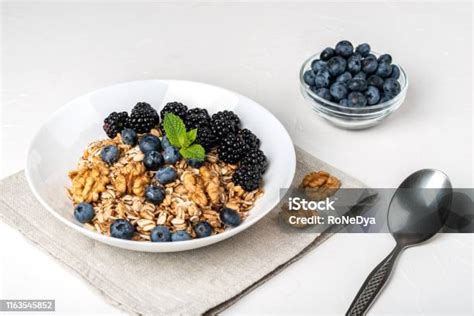 건강한 아침 식사 홈메이드 그래놀라 뮤즐리 블랙베리 블루베리 견과류 꿀 민트가 있는 시리얼을 흰색 바탕에 흰색 그릇에 담았습니다