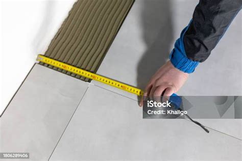 타일러 작업자는 속눈썹 타일 레벨링 시스템 개조 또는 재건설 건물 개념으로 접착 접착제 위에 회색 세라믹 타일을 배치하거나