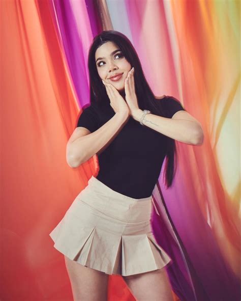 A Woman Posing In Front Of A Colorful Curtain With Her Hands On Her Face And Looking At The Camera