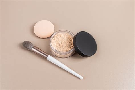 베이지 배경에 자연스러운 톤의 드라이 파우더 둥근 스폰지 아름다운 메이크업 브러시가 있는 오픈 화장품 항아리 장식 화장품의 개념