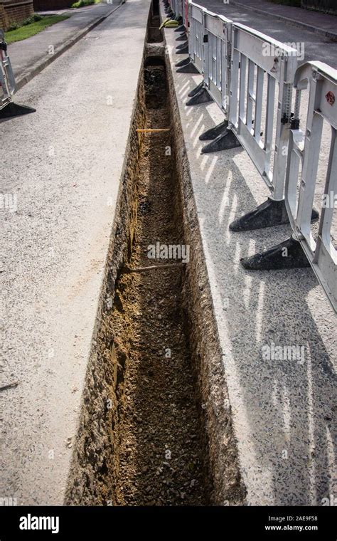 Long Deep Trench Through Road Surface Cordoned Off By Plastic Barriers