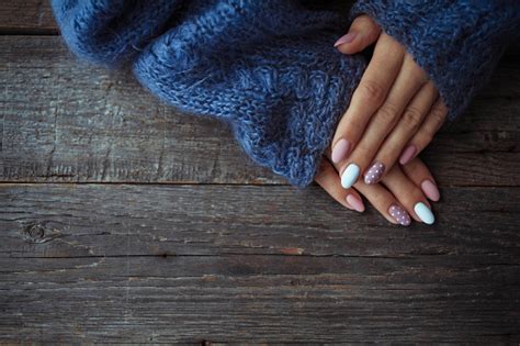 여성은 나무 배경에 보라색 니트 스웨터에 아름다운 매니큐어와 손입니다 가을 트렌드 광택 베이지색과 흰색 물방울 무늬가 젤 폴리시 셸락을 곁들인 손톱에 장식되어 있습니다