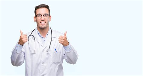잘생긴 젊은 의사 남자 성공 기호 손으로 긍정적인 제스처를 하 고 웃 고 행복 한 엄지 쾌활 한 식 우승자 제스처와 카메라를 보면 건강관리와 의술에 대한 스톡 사진 및 기타