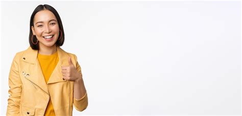 Красивая корейская девушка улыбается показывая большой палец вверх как жест рекомендуя