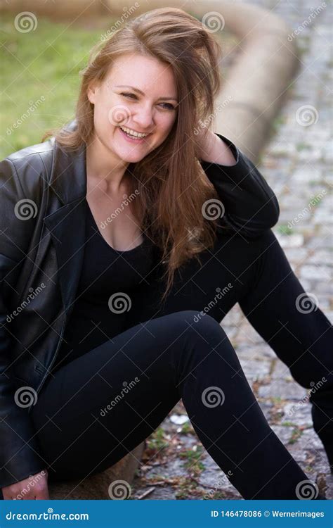 Young Woman In Black Leather Jacket Sitting Outdoors In Park Stock