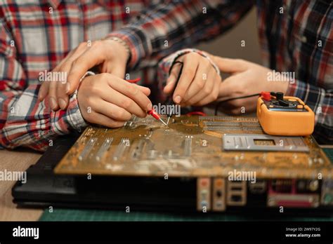 Close Up Of Father And Son Hands Testing Laptop Motherboard Using Multimeter DIY Stock Photo