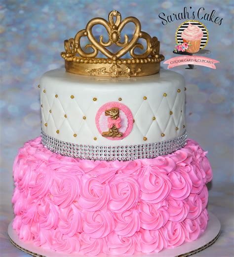 There Is A Cake With Pink Frosting And A Gold Crown On Top
