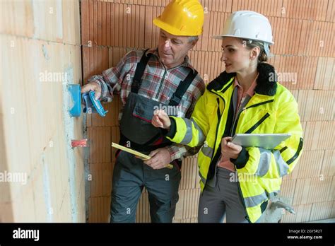 Male And Female Construction Engineer Checking A Pipe Inserted In Wall Of A Building Stock Photo