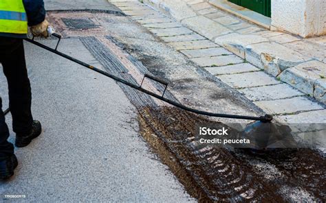 아스팔트 도로의 부분 수리 작업자는 아스팔트 표면에 역청을 분무합니다 도로 유지 보수 작업자는 역청 혼합물을 청소된 사람에게 분무합니다 개발에 대한 스톡 사진 및 기타